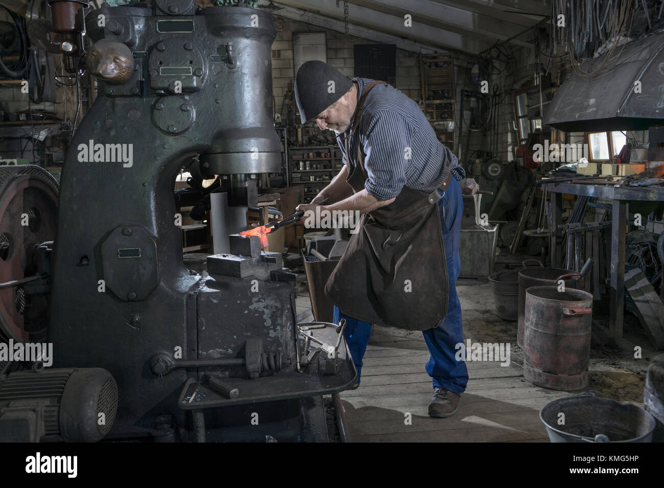 Blacksmith hammering red hot iron bar in hammer machine at workshop ...
