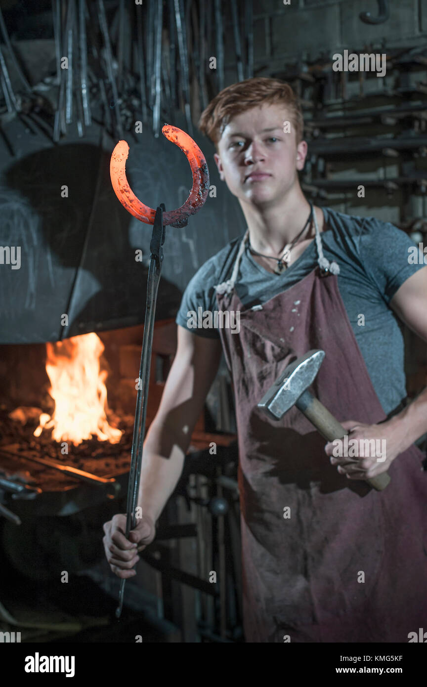Apprentice blacksmith with hammered red hot horseshoe at workshop Stock ...