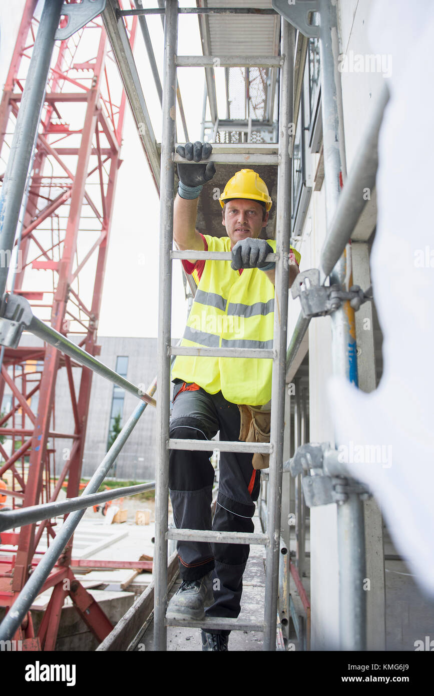 Construction worker at building site climbing up a ladder Stock Photo ...