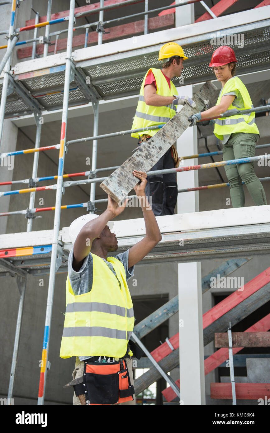Construction workers passing wooden plank at building site Stock Photo ...