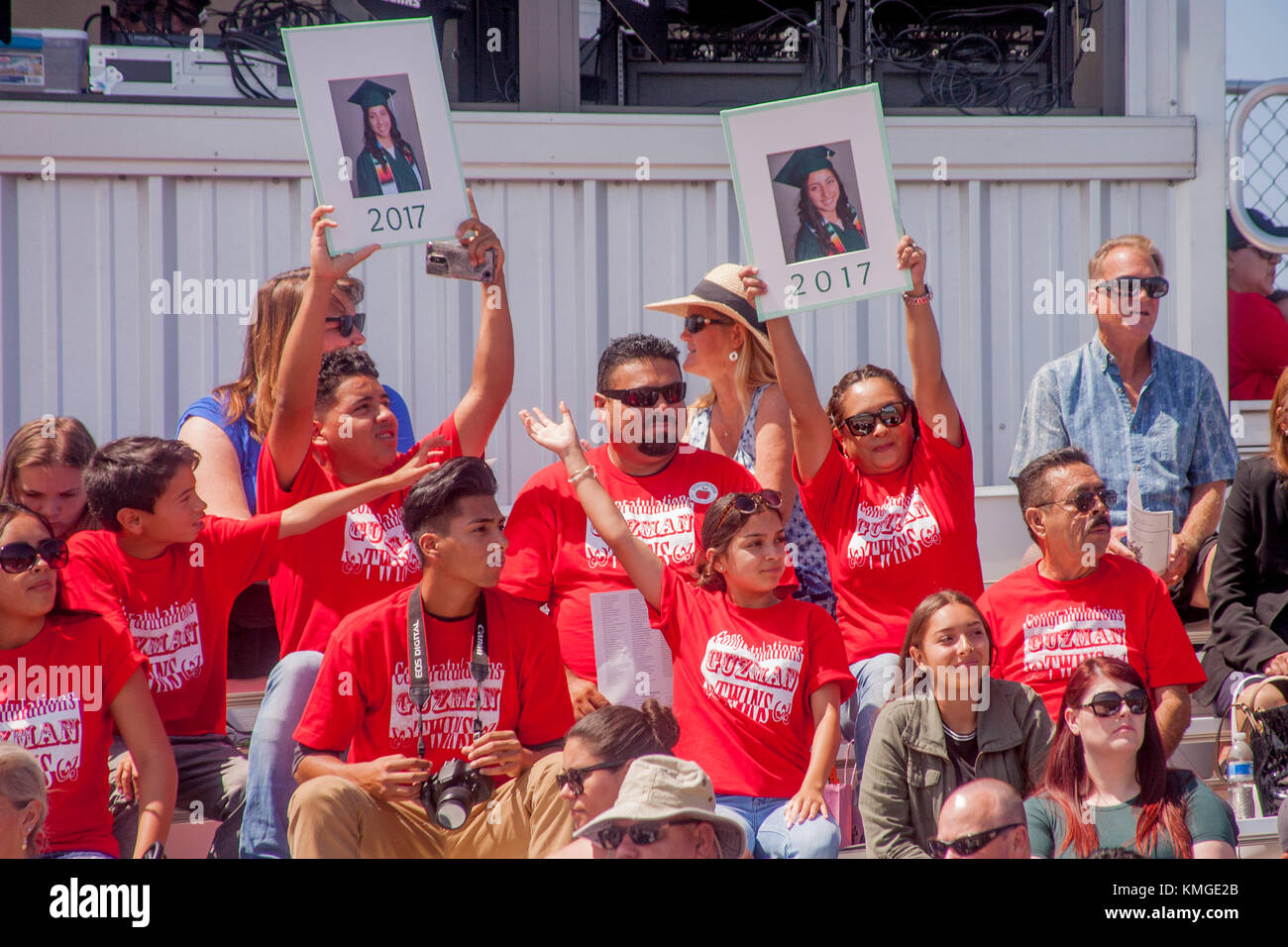 Parents of Hispanic high school graduates in red commemorative T shirts ...