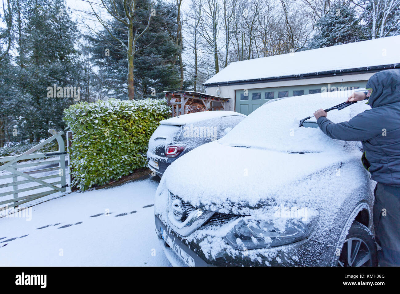 A person clearing snow off cars on a driveway before the morning ...