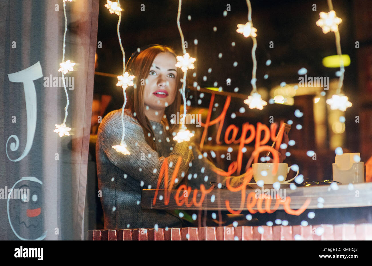 Young beautiful woman sitting in cafe, drinking coffee. Magic snowfall ...