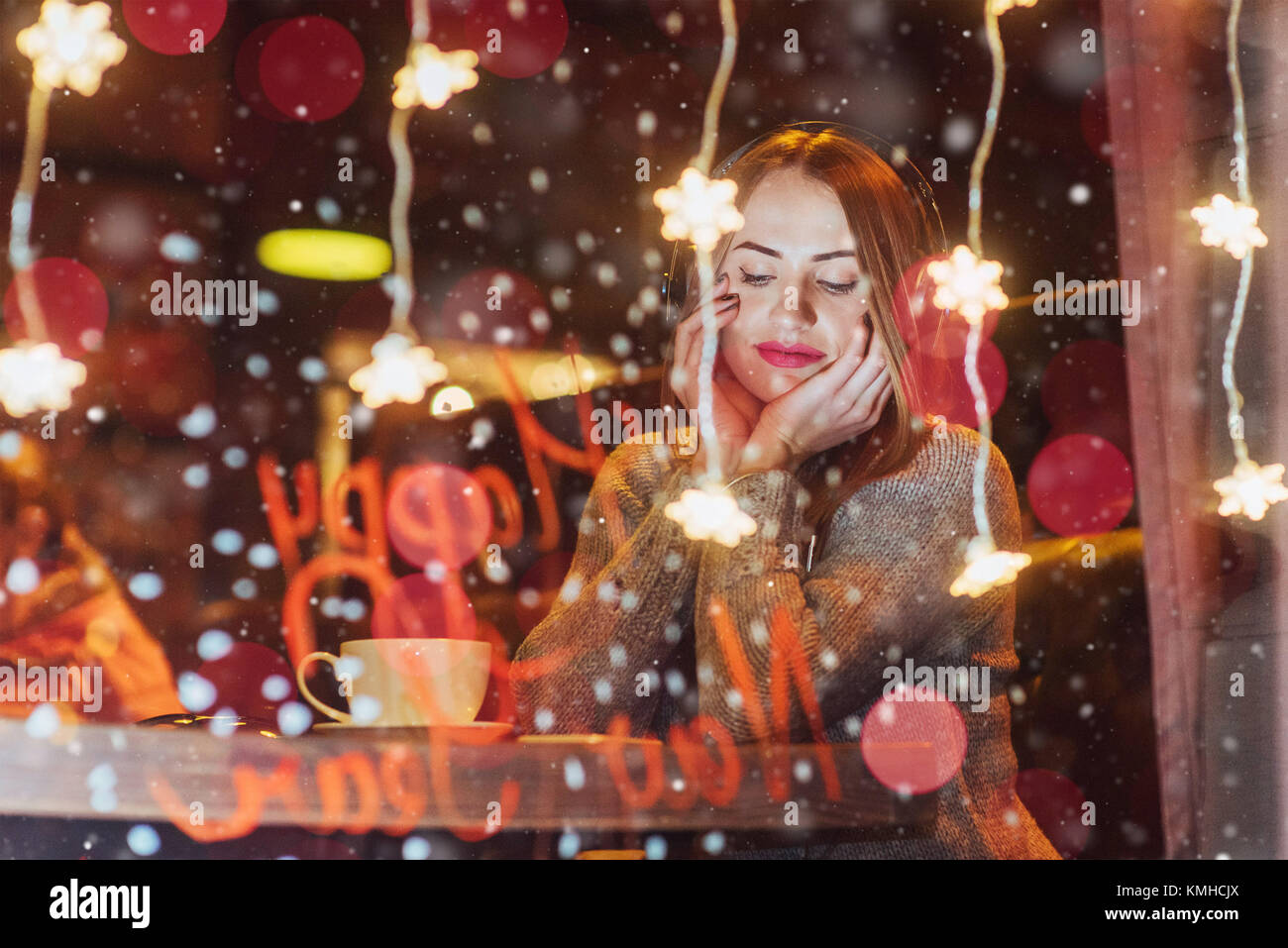 Young beautiful woman sitting in cafe, drinking coffee. Magic snowfall ...