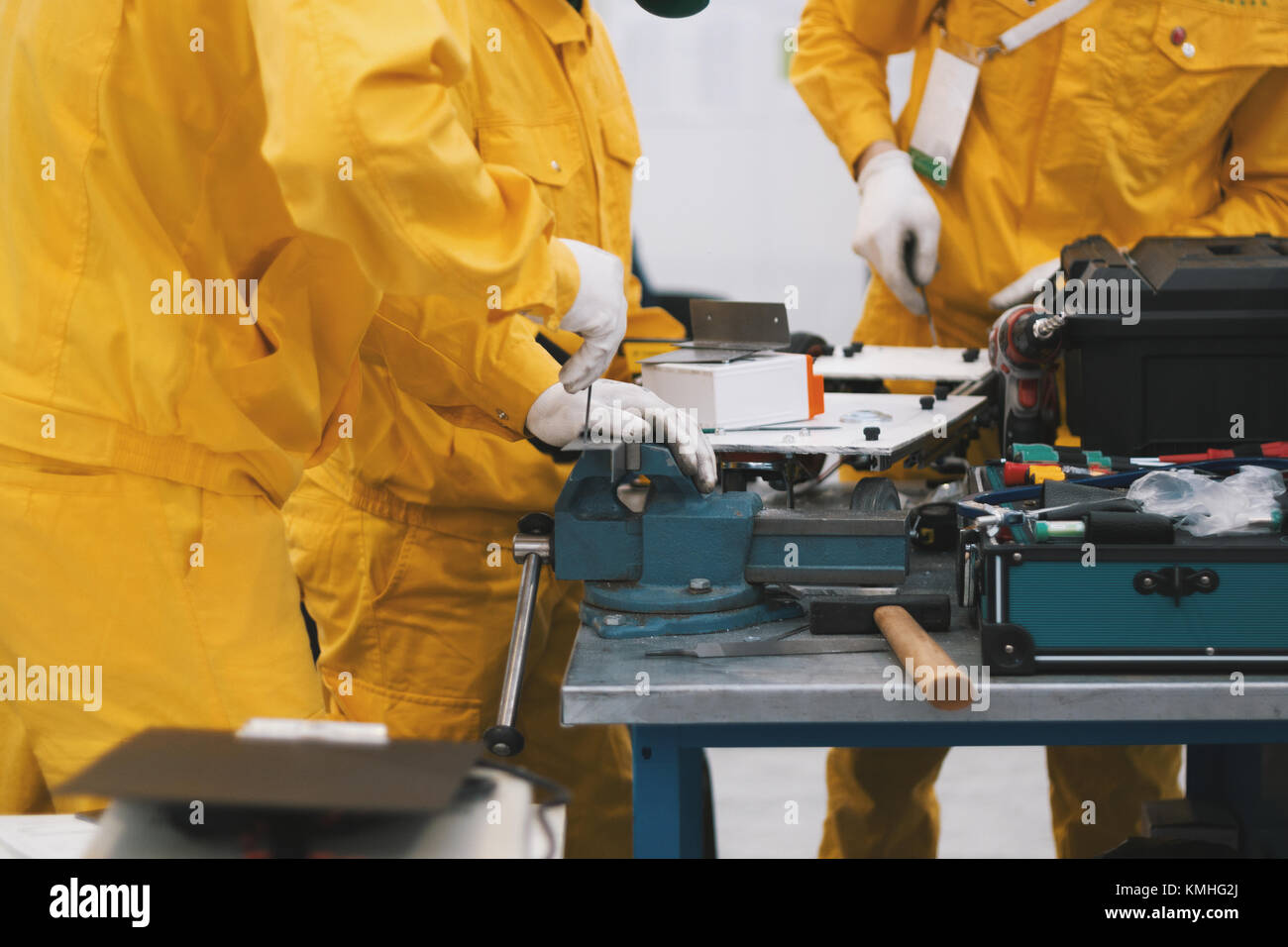 Engineers and workers in yellow overalls working in metal workshop ...