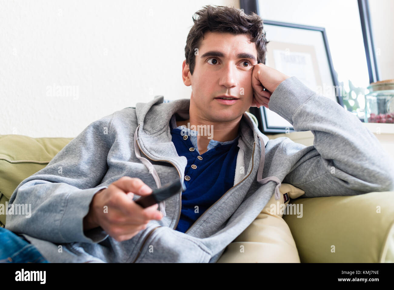 Portrait of young man sitting on the sofa with the remote control in ...