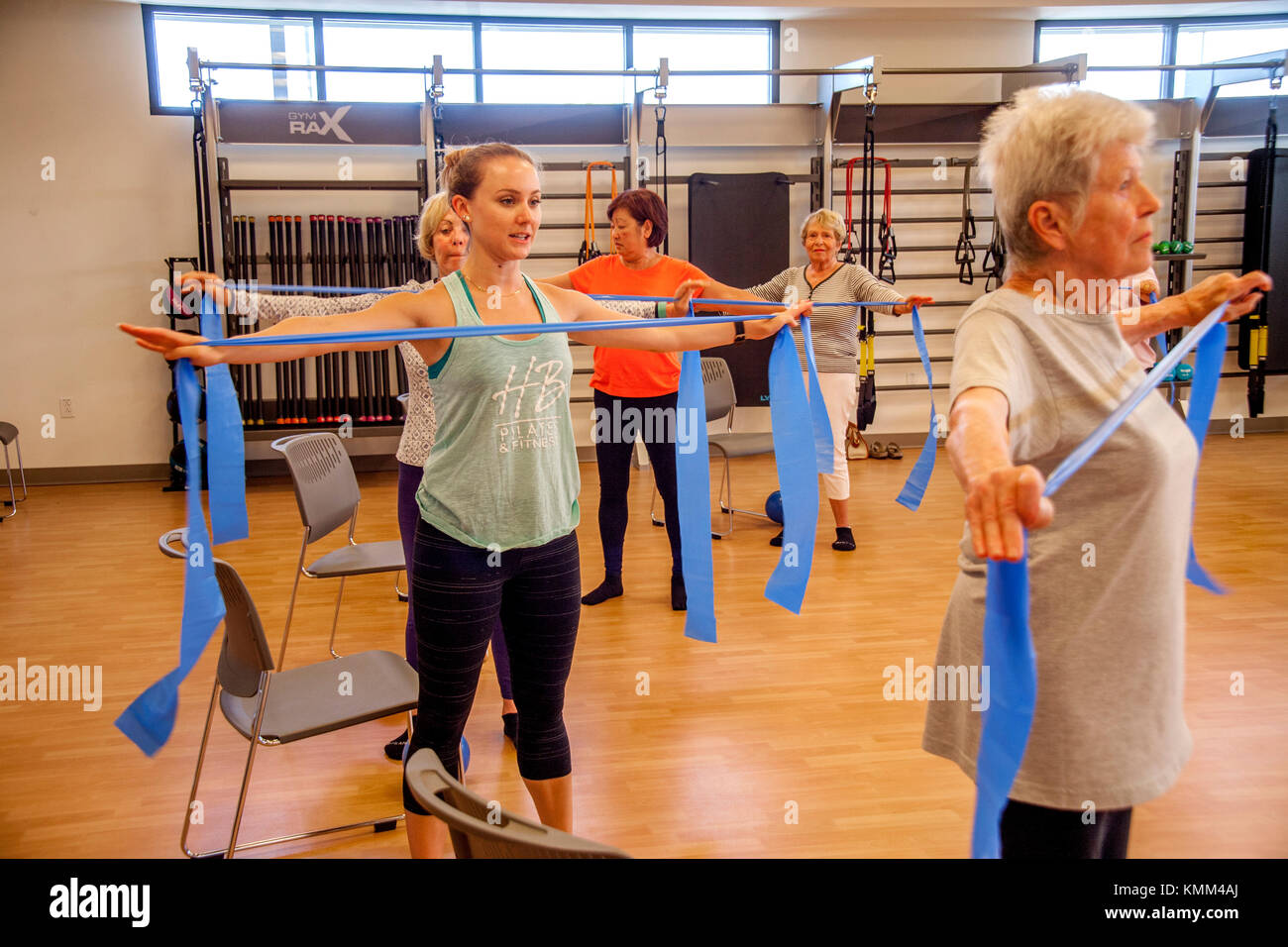 A young adult instructor leads senior women in stretch band exercises ...