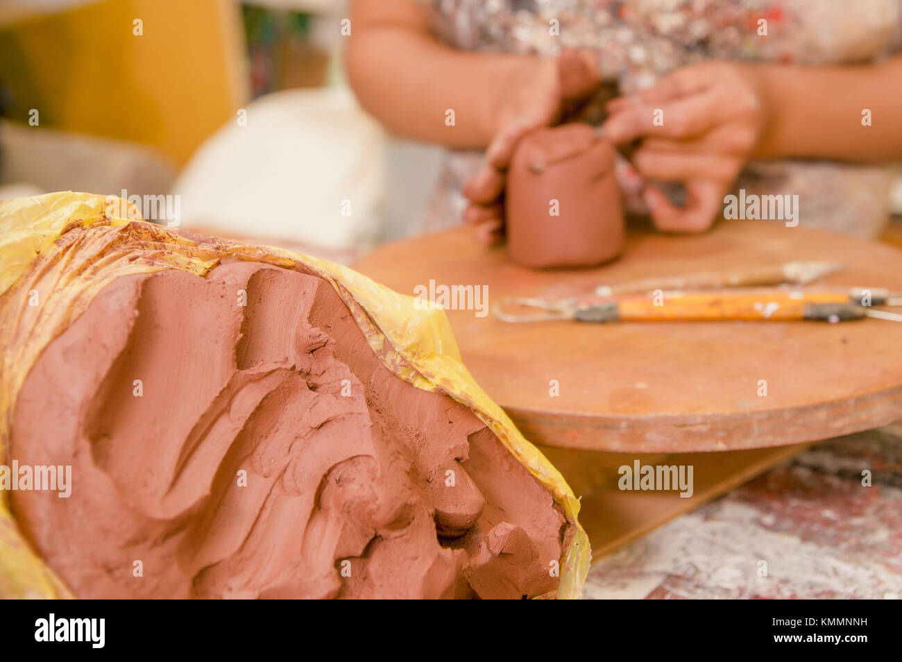 Close up of a clay mass with a blurred woman ceramist behind working on ...