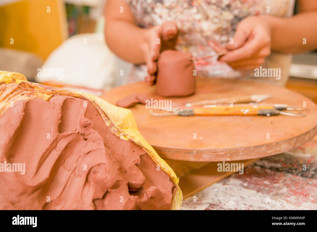 Close up of a clay mass with a blurred woman ceramist behind working on ...