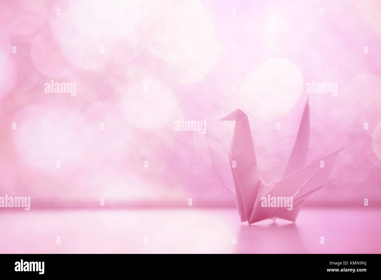 origami paper bird on the bright-lit glass window with pink solf light ...