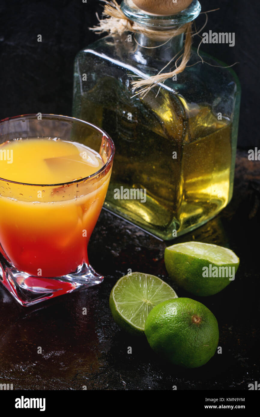 Glass of tequila sunrise cocktail, served with bottle of tequila anejo ...