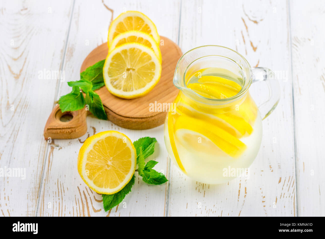 A pitcher with a cold lemonade on a white wooden background surrounded ...