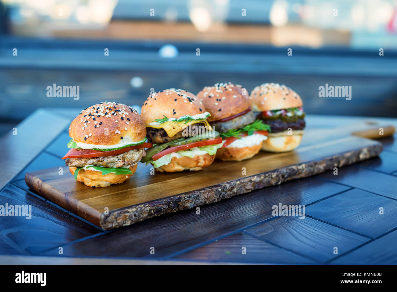 Four burgers on wooden board in restaurant Stock Photo - Alamy