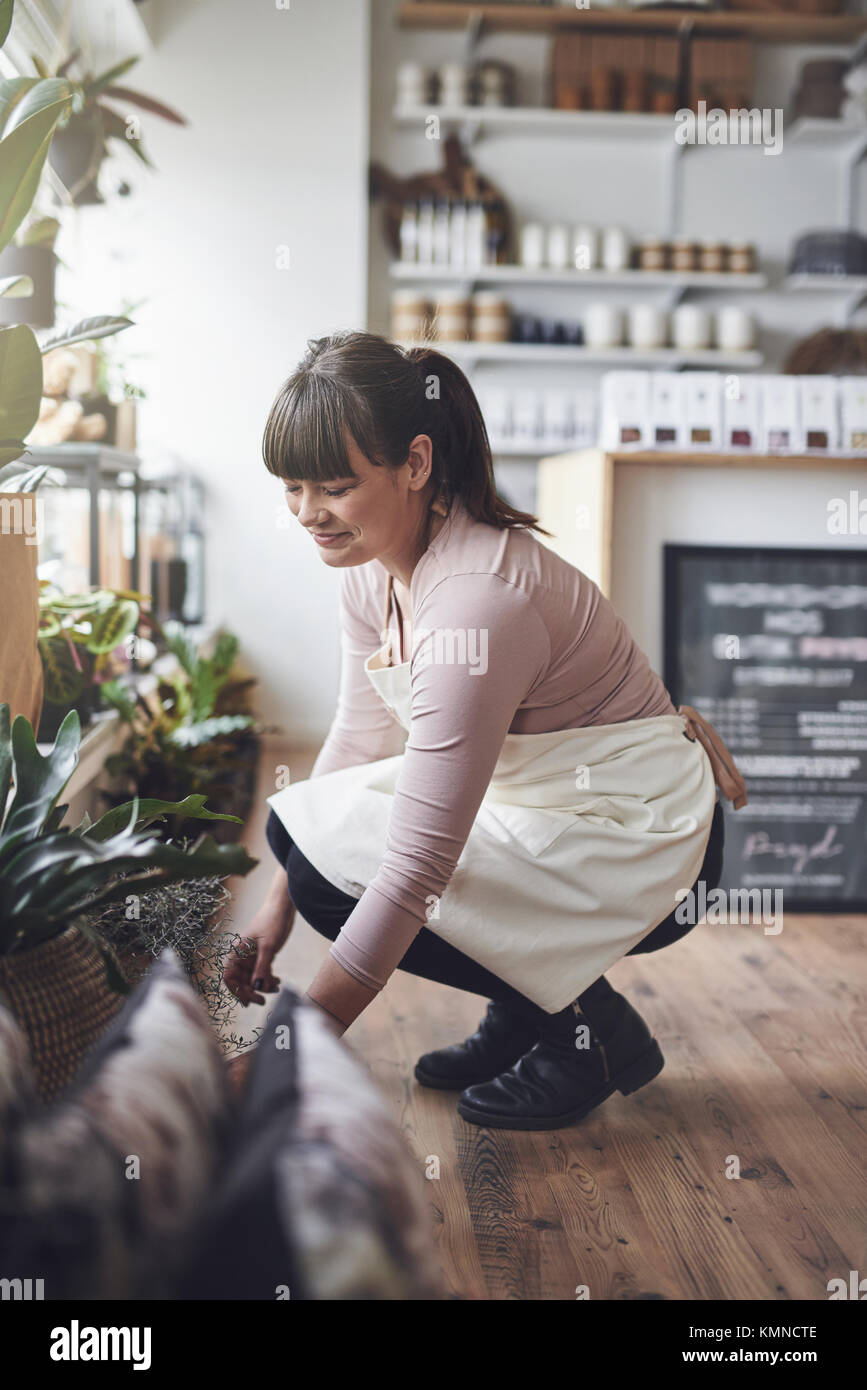 Smiling young female florist busy working in her flower shop arranging ...