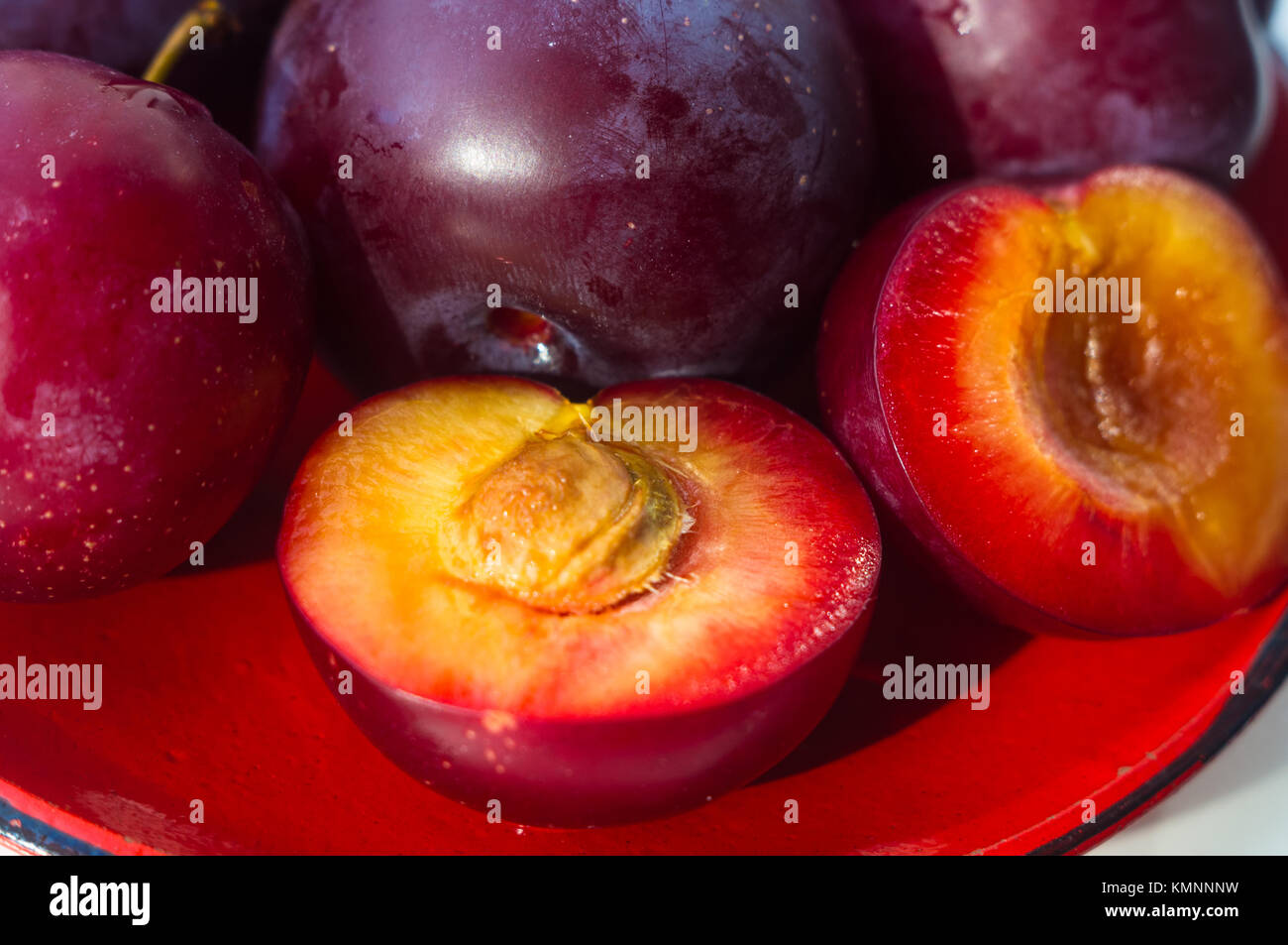 fresh plum fruit with cut plum slices in the red saucer on white ...