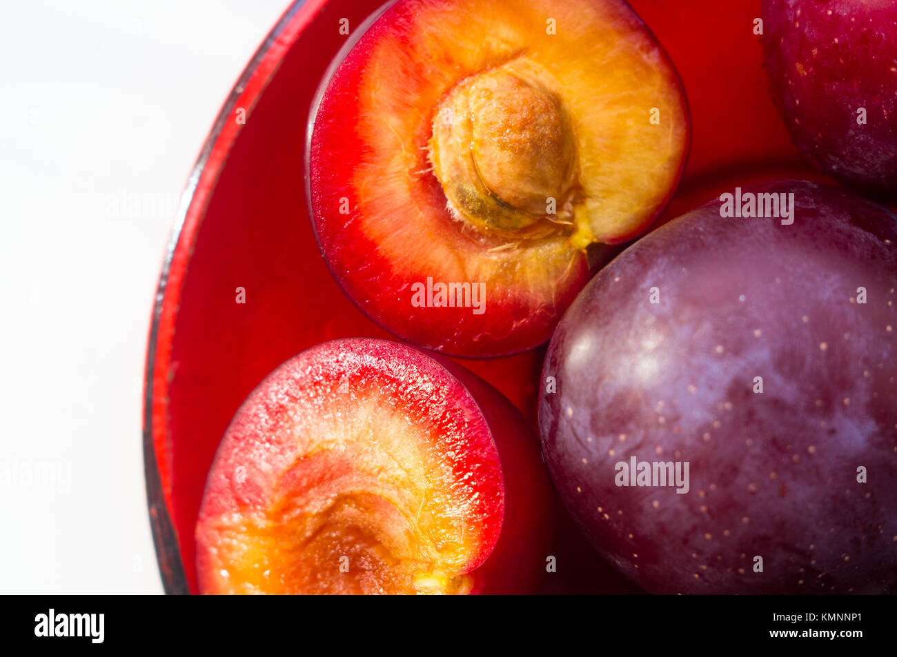 fresh plum fruit with cut plum slices in the red saucer on white ...