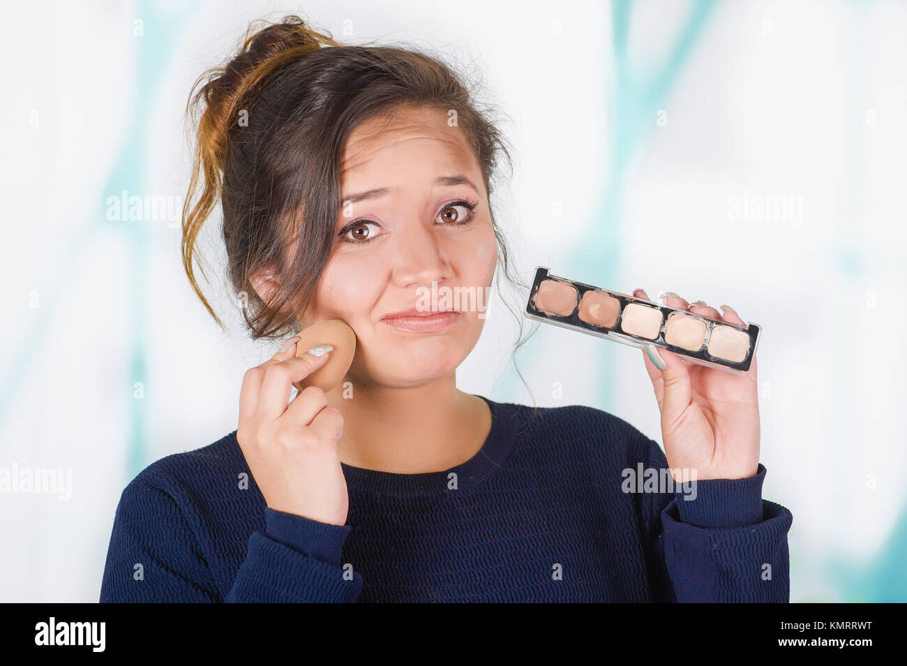 Close up of worried young woman holding a make up palette and doing ...
