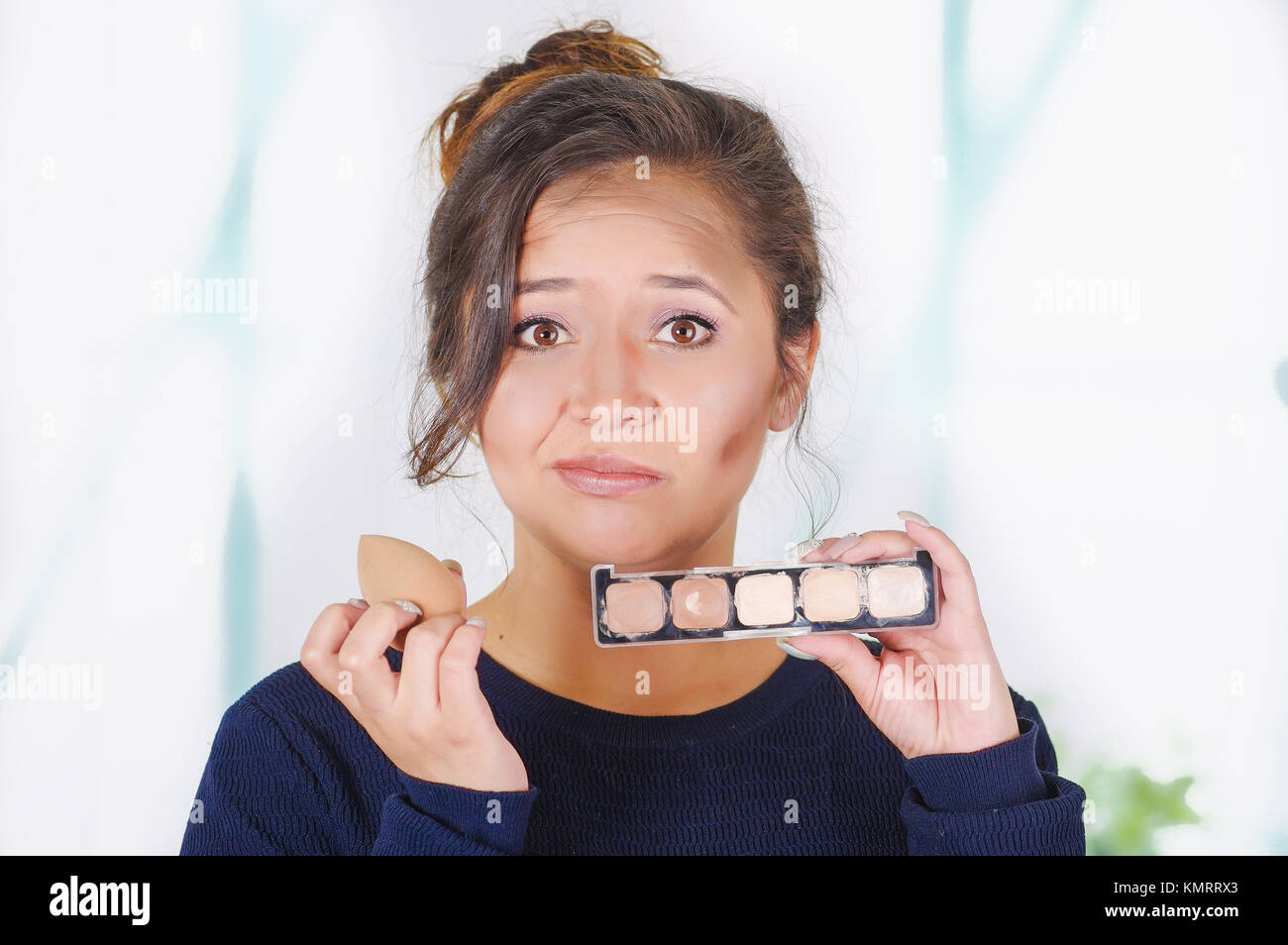 Close up of worried young woman holding a make up palette and doing ...