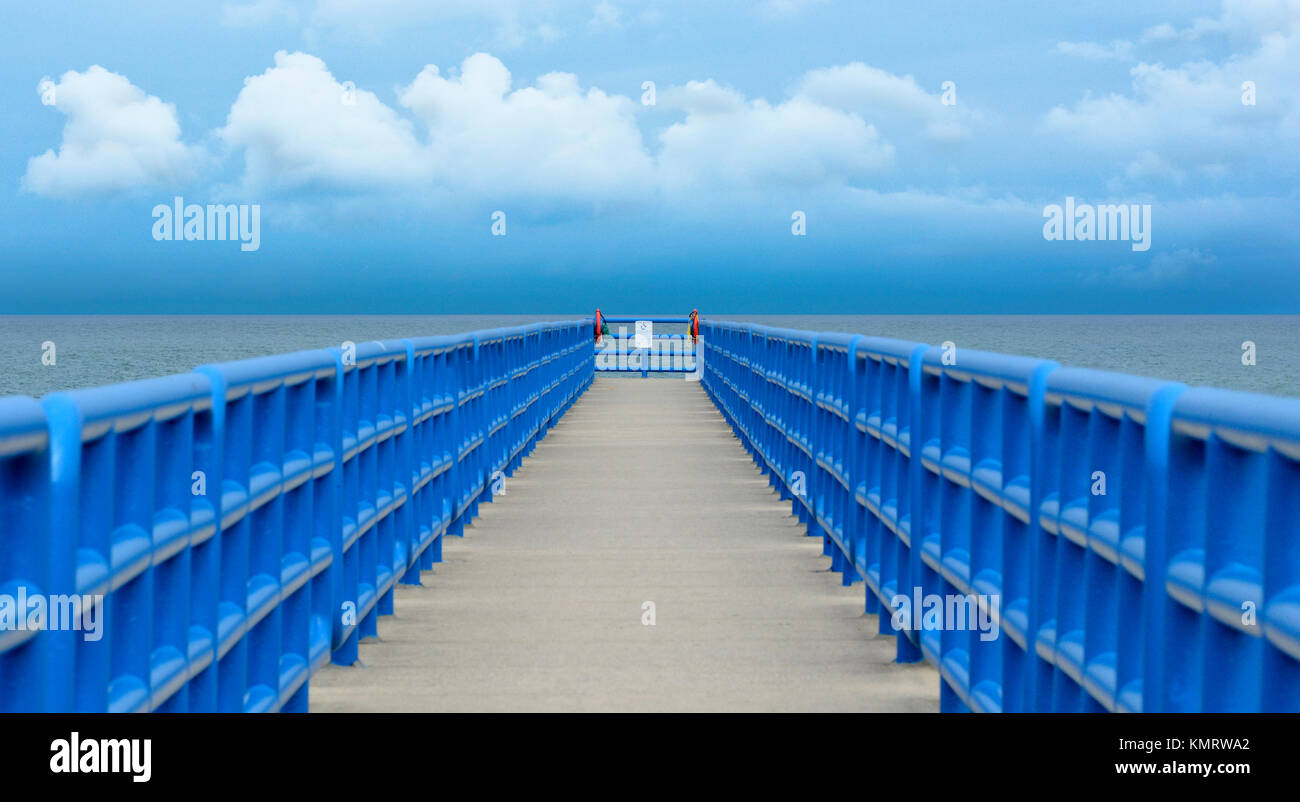 Horizontal photo of a blue pier stretching across blue water against a ...