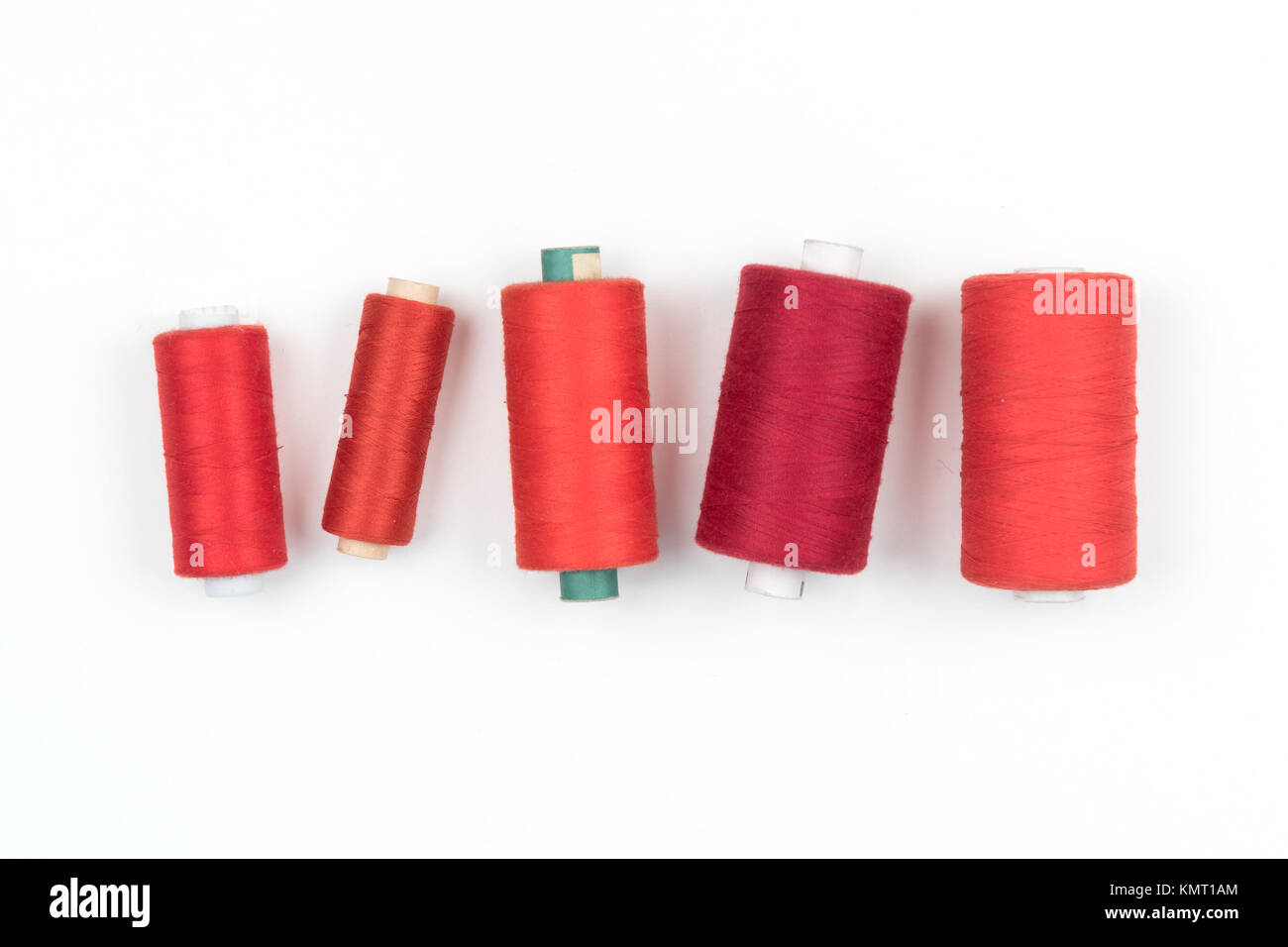Row of five red colour thread coils on a white background, sewing and ...