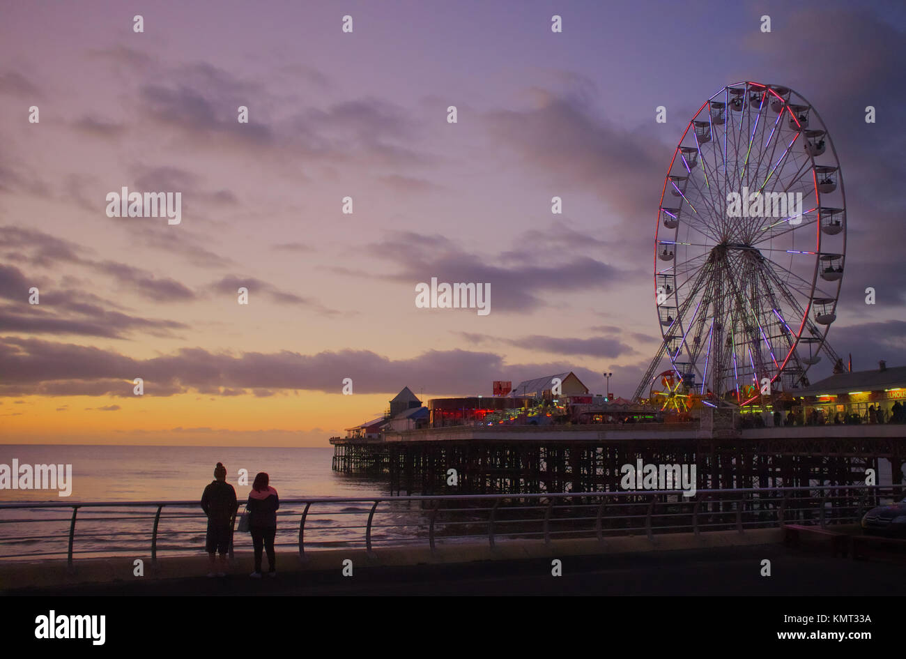 Two people watching the sunset and Illuminated Big wheel ride on ...