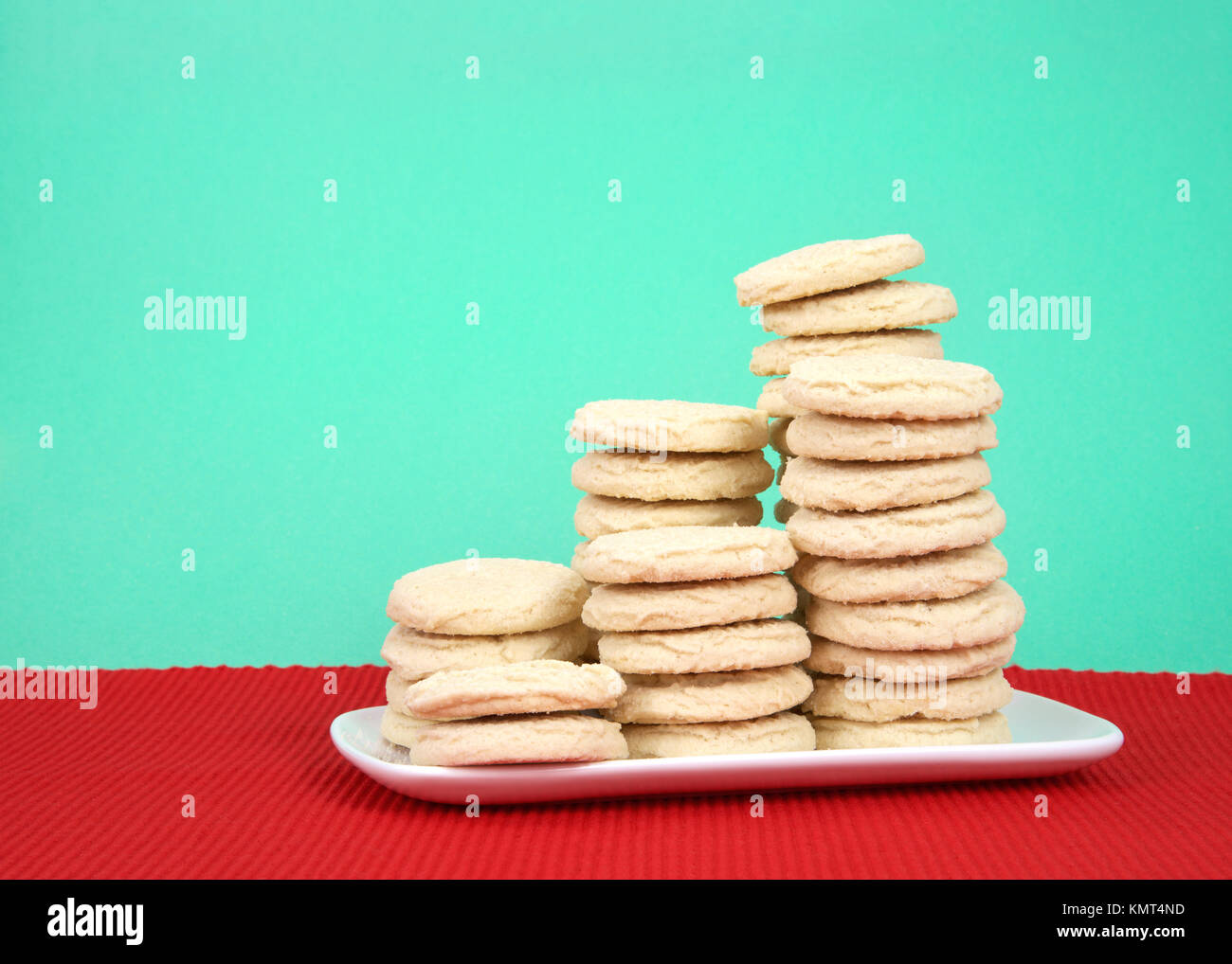 Sugar cookies stacked at multiple heights on a white rectangular plate ...