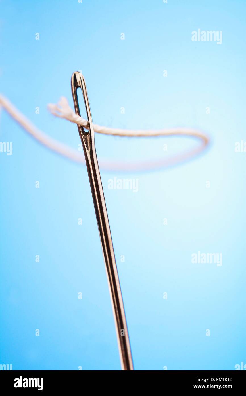 White thread going through needle eye closeup on blue background Stock ...