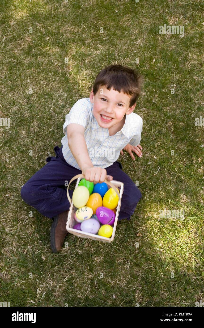a boy sits on the lawn showing off his white easter basket full of ...