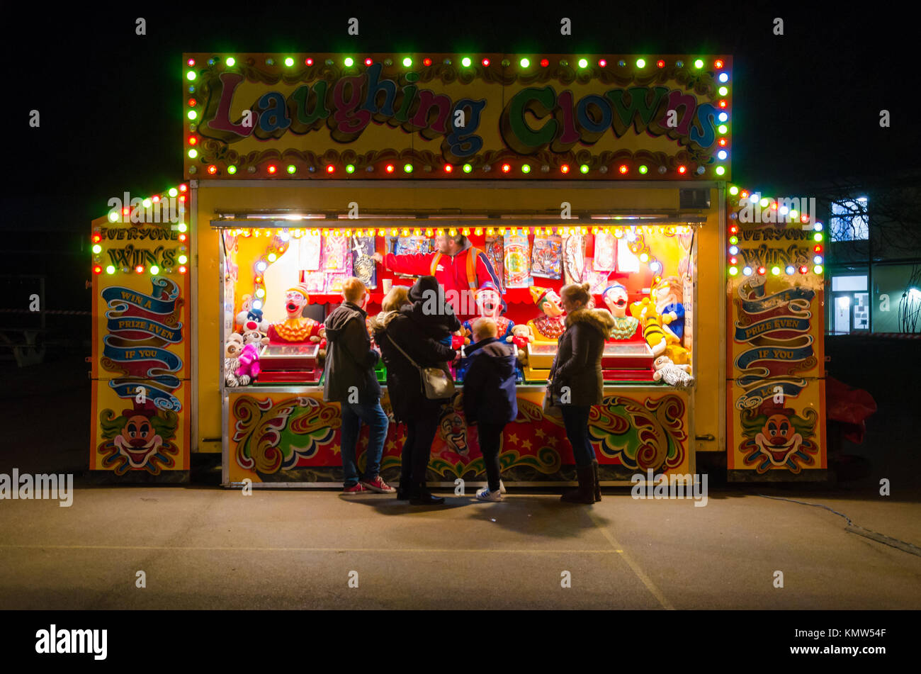 A family stop and play a laughing clowns game at a stall at a fair ...