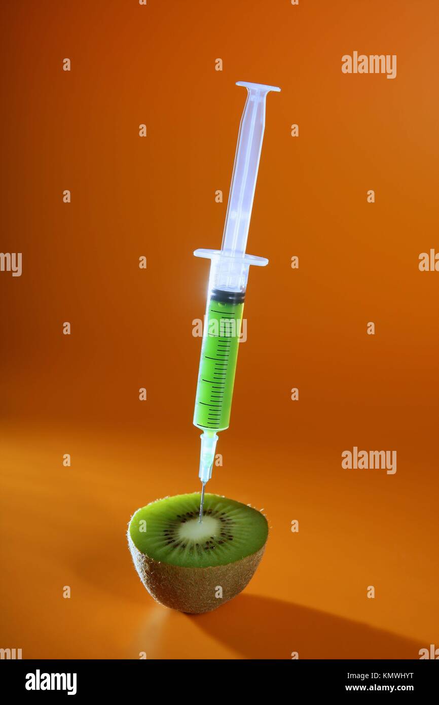 Injection with syringe to a green kiwi fruit over orange background ...