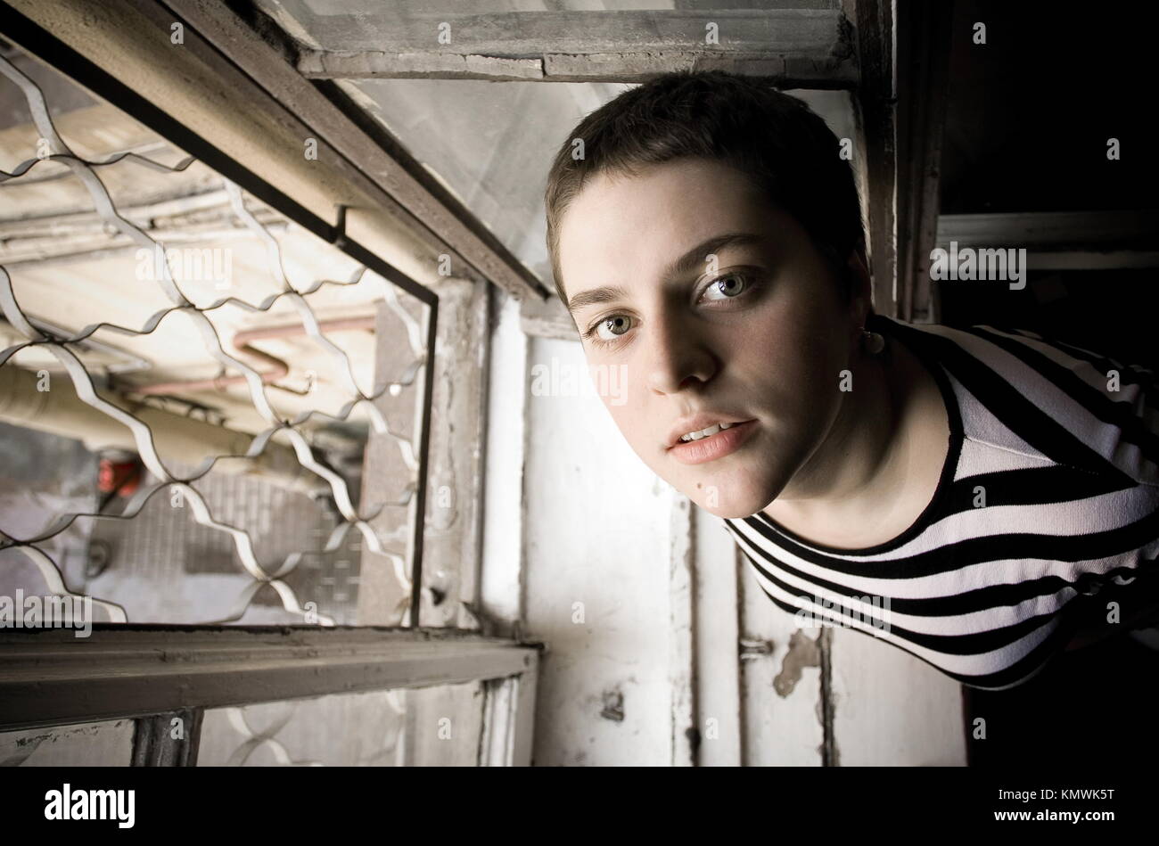 A young girl with a short hair stays by the window and looks up at the ...