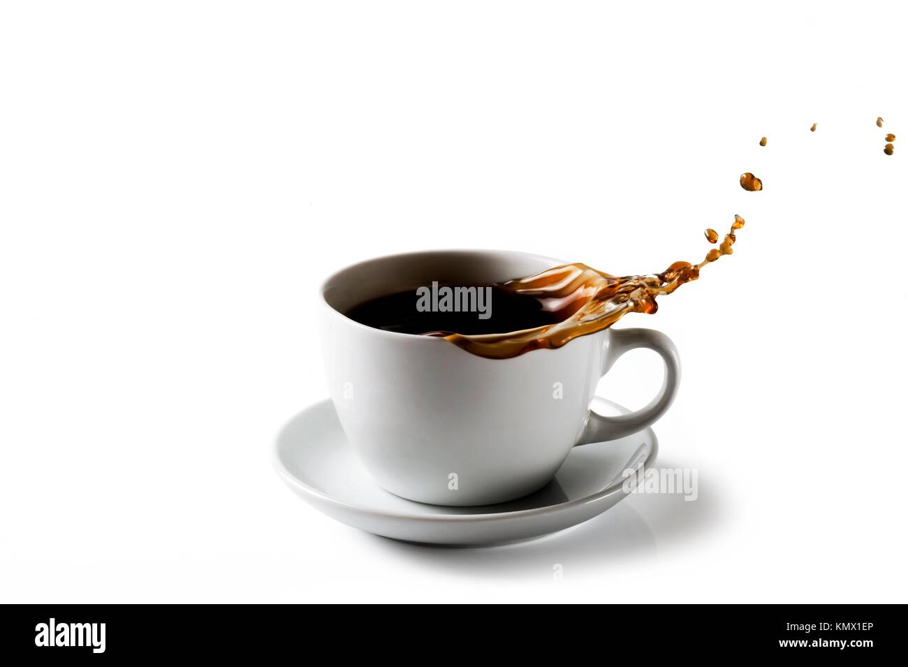 A cup of coffee with splashing coffee pouring out on to a white ...