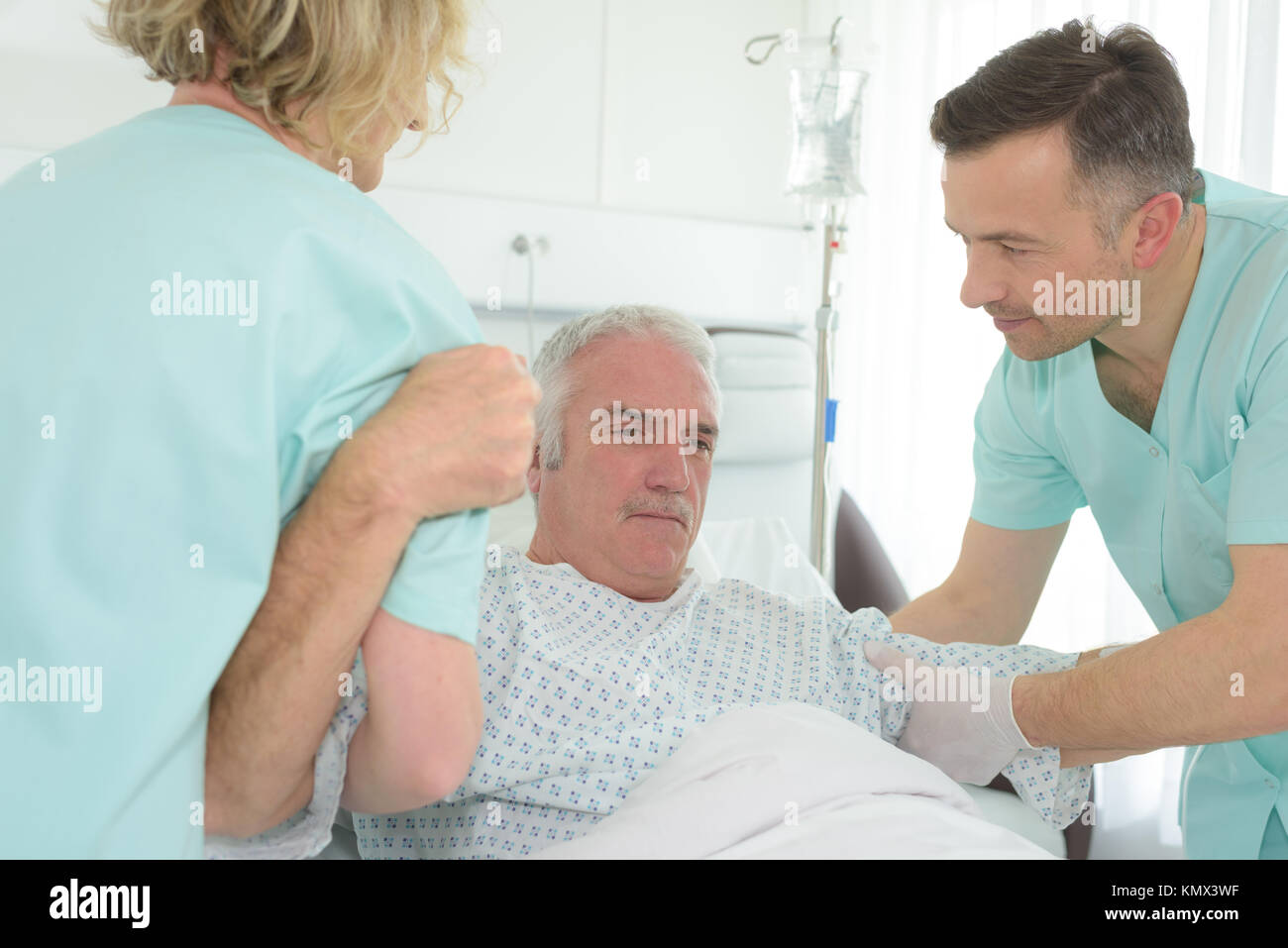 Medical workers helping patient rise from bed Stock Photo - Alamy