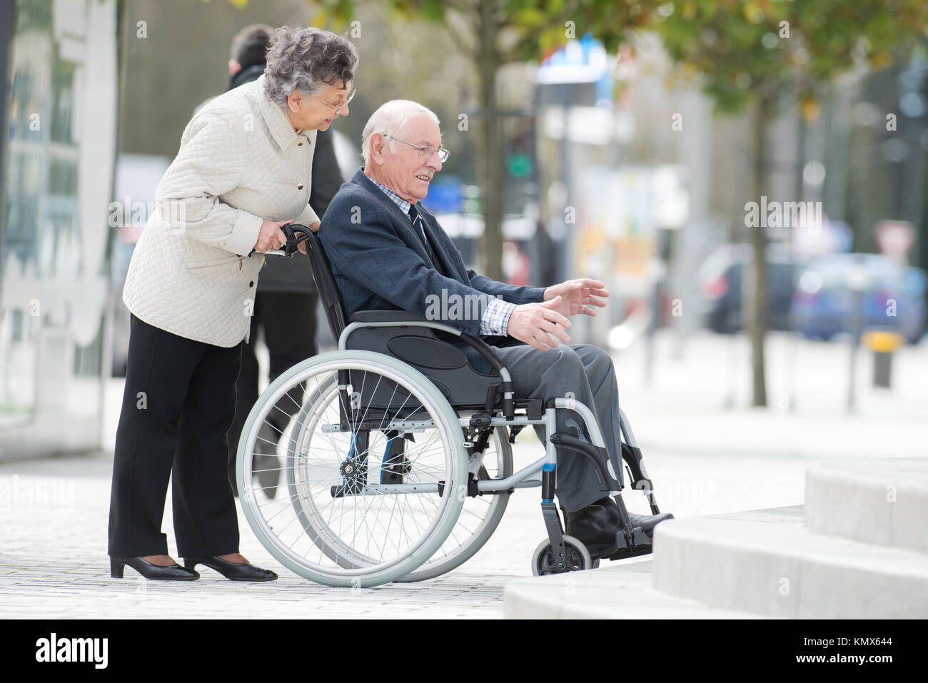 senior lady pushing her husband in his wheelchair Stock Photo - Alamy
