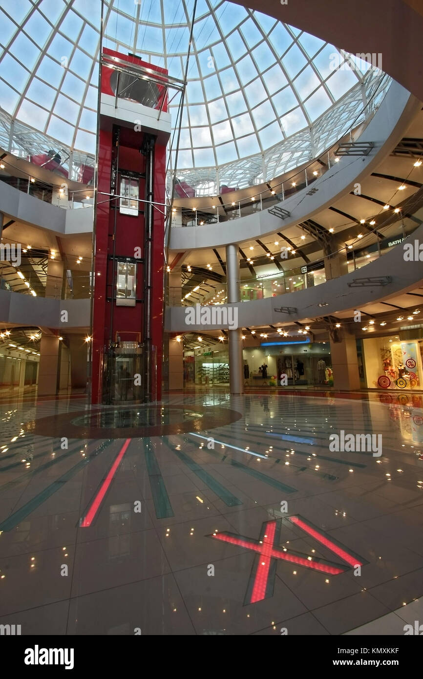 Huge hall of modern shopping centre with the glass lift, hours on a ...