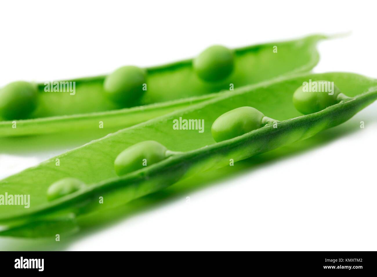 A close-up of a pea pod split open revealing peas on white background ...