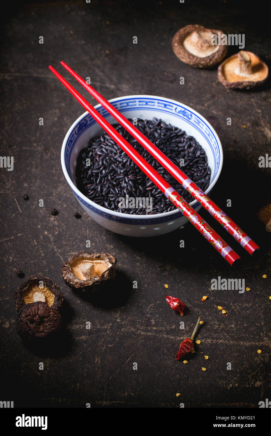 Porcelain bowl of uncooked black rice, served with dry shiitake ...