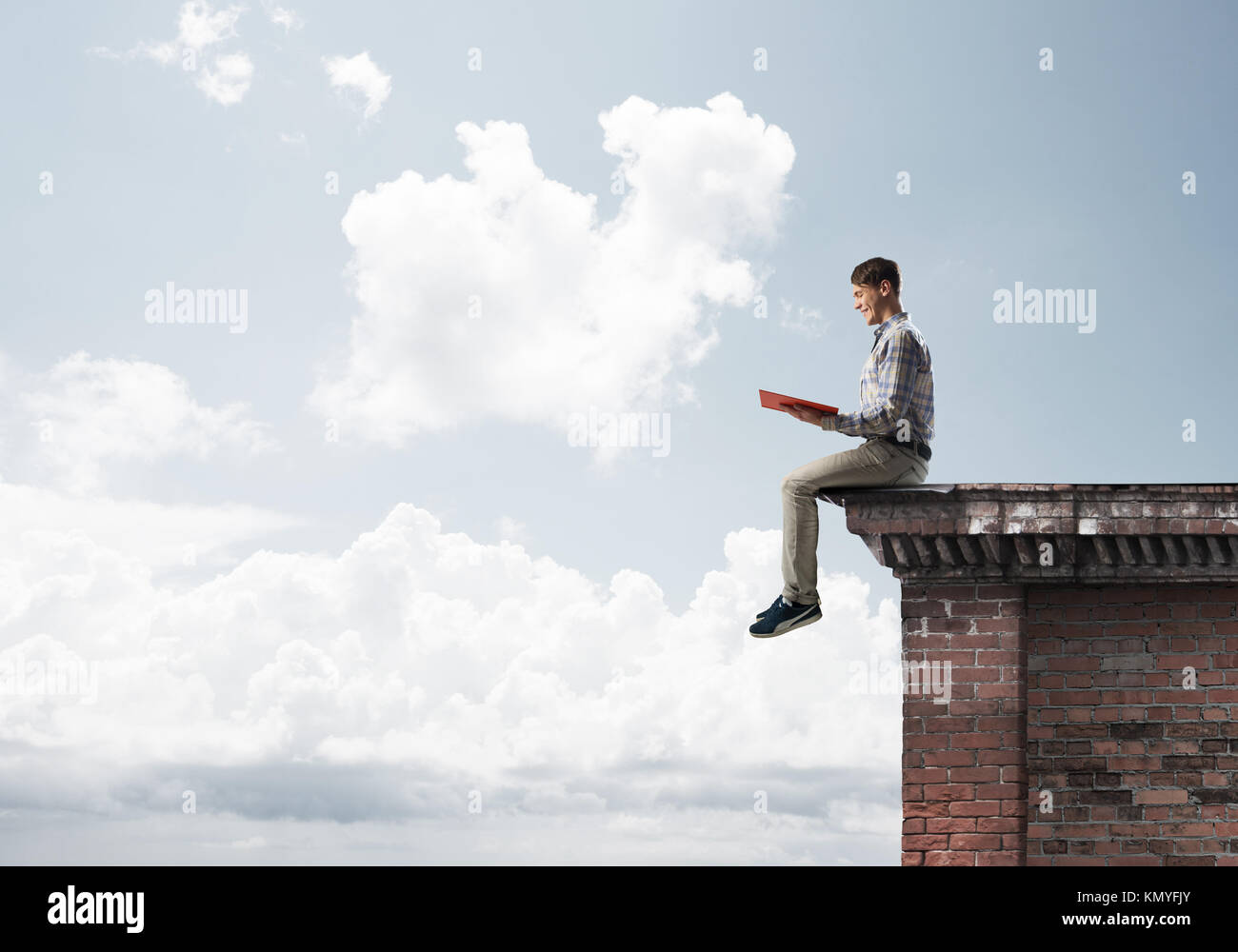 Man on roof edge reading book and cloudscape at background Stock Photo ...