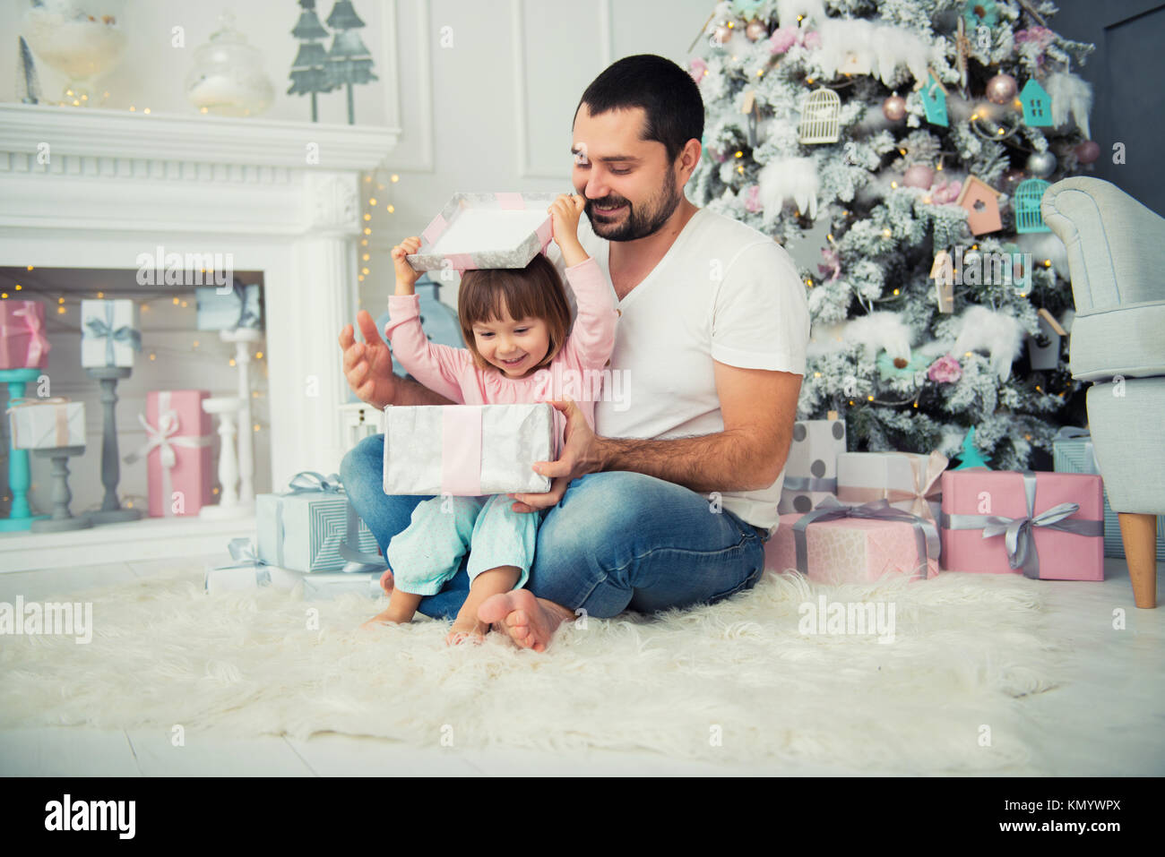 Dad and daughter are sitting and opening a Christmas present near the ...