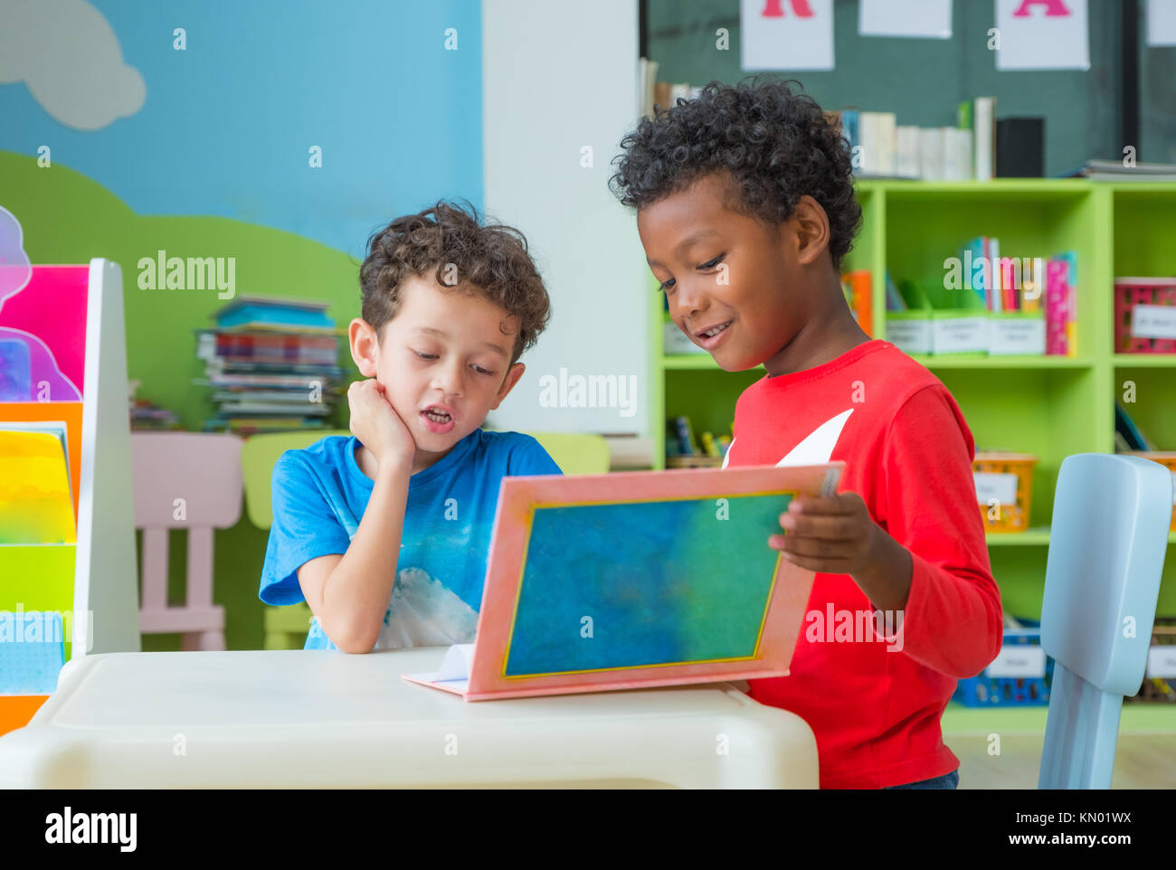 Two boy kid sit on table and reading tale book in preschool library ...