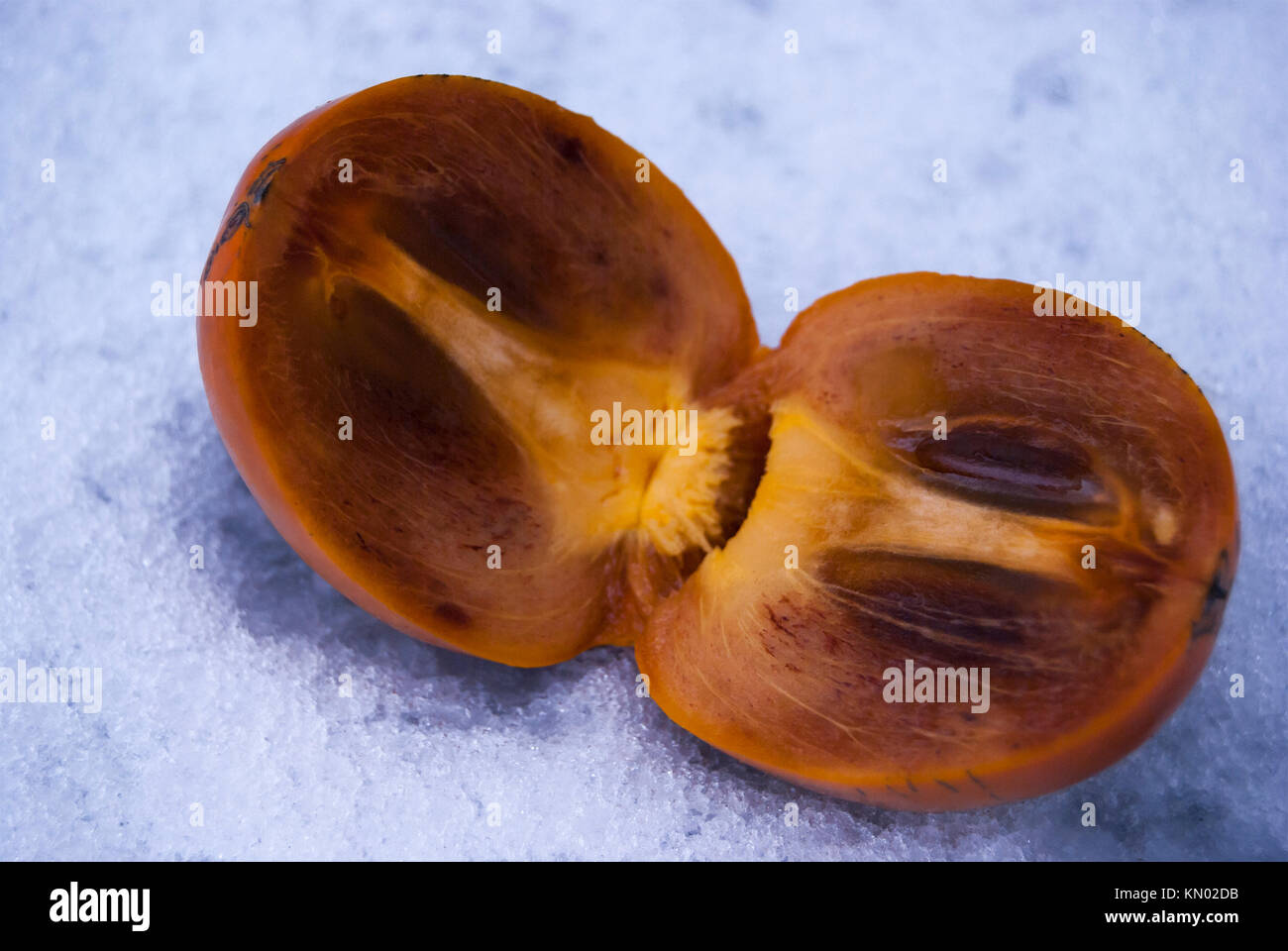 Persimmon, cut in half, lies on the snow on the table Stock Photo - Alamy