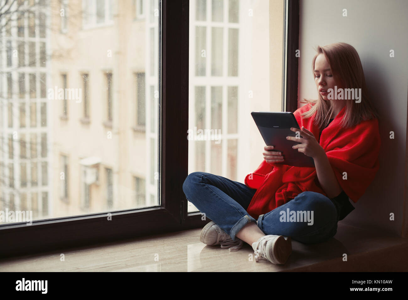 Portrait of a young girl reading an e-book at the window Stock Photo ...