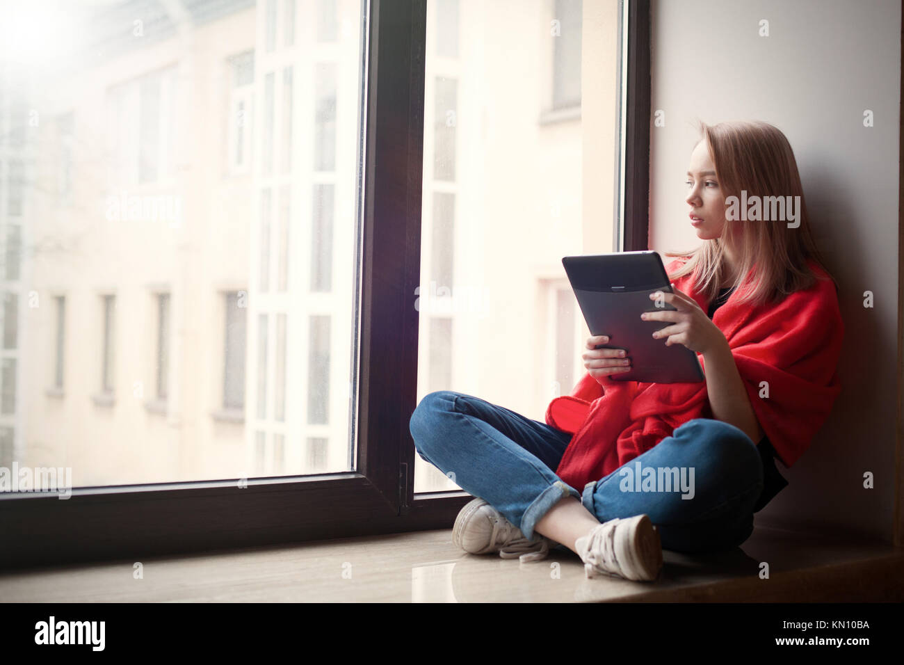 Portrait of a young girl reading an e-book at the window Stock Photo ...