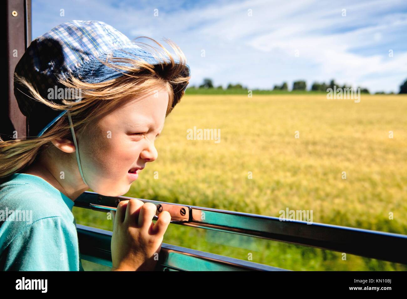 boy with long blond hair and hat looking out the train window Stock ...
