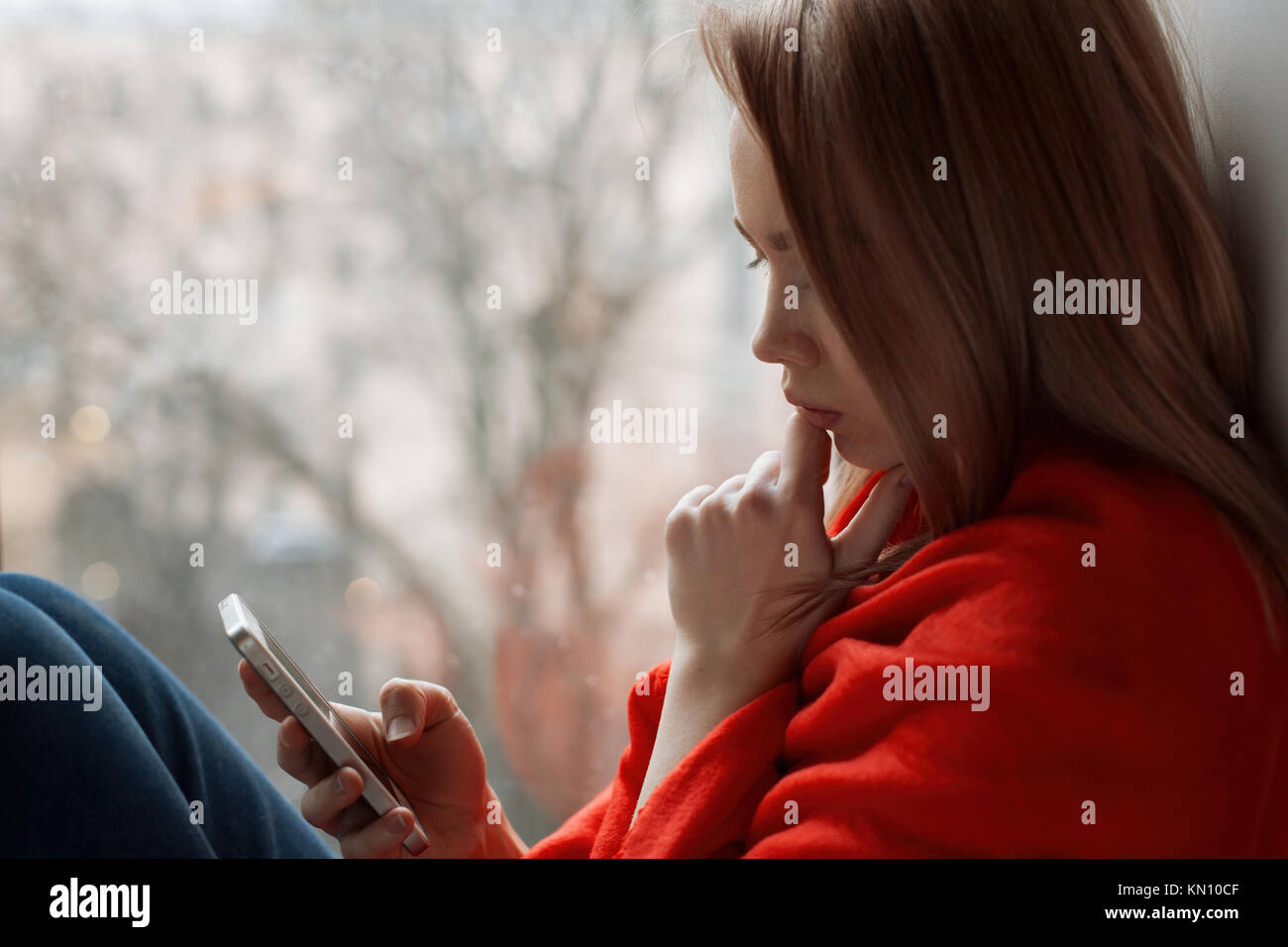 Portrait of a young girl reading a message on a telephon sitting by the ...