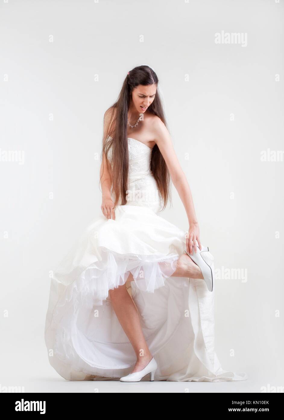 bride in wedding dress taking off her shoe checking her hurting foot ...
