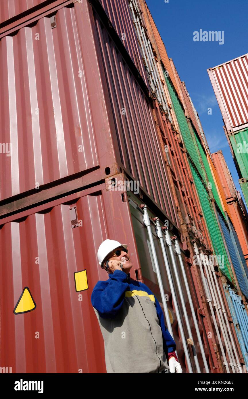 port worker with stacks of shipping containers in background ...