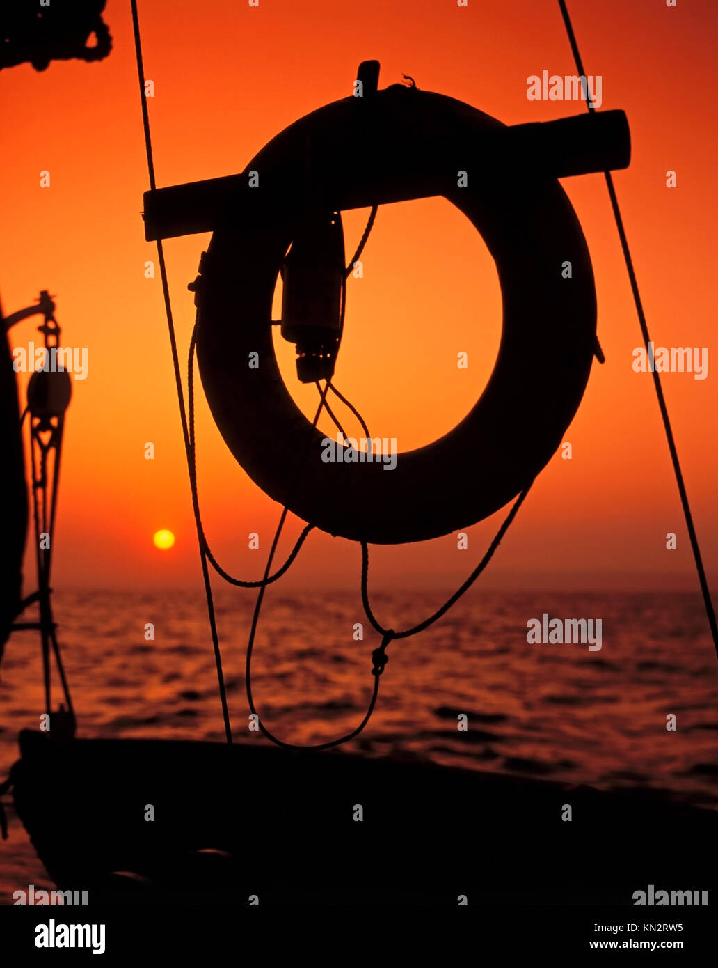 Sunset at sea looking through the silhouette of rigging and lifebuoy of ...