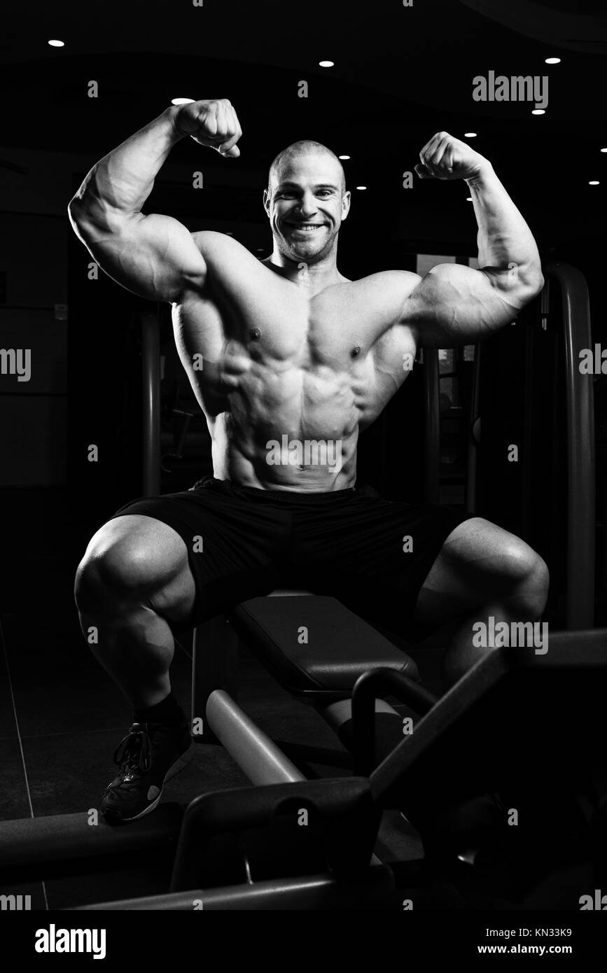 Young Man Sitting Strong In The Gym And Flexing Muscles - Muscular ...