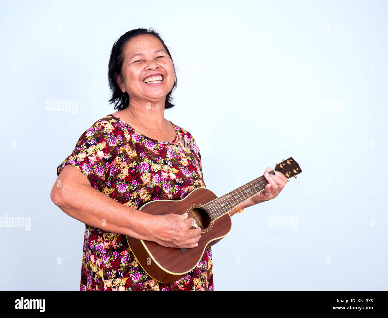 Asian senoir woman playing ukulele with big smile on white background ...